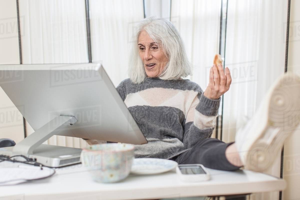 Portrait of senior woman sitting at computer with foot on desk - Stock ...