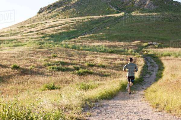 Rear view of young male runner running up hillside track - Royalty-free ...