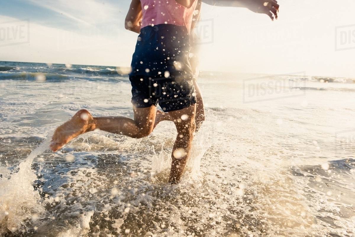 Young man running in sea, low section - Stock Photo - Dissolve