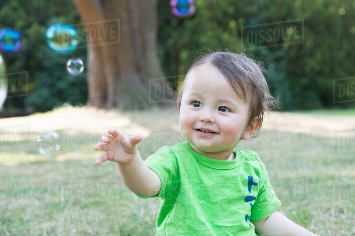 Portrait of cute baby boy reaching for bubbles in park - Royalty-free ...