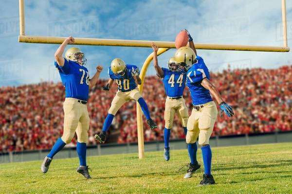 Team of teenage and adult American footballers playing in stadium next ...