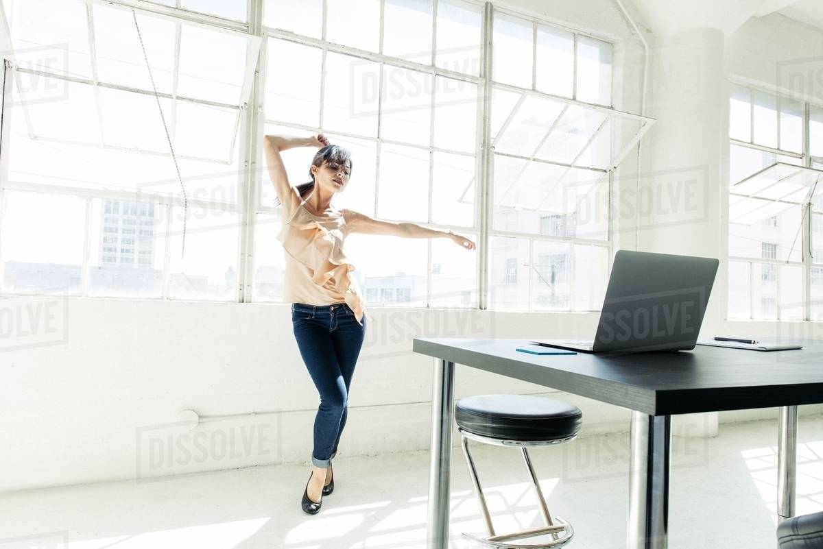 Businesswoman dancing by office window - Stock Photo - Dissolve