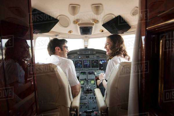 Rear view of male and female pilot chatting in cockpit of private jet ...