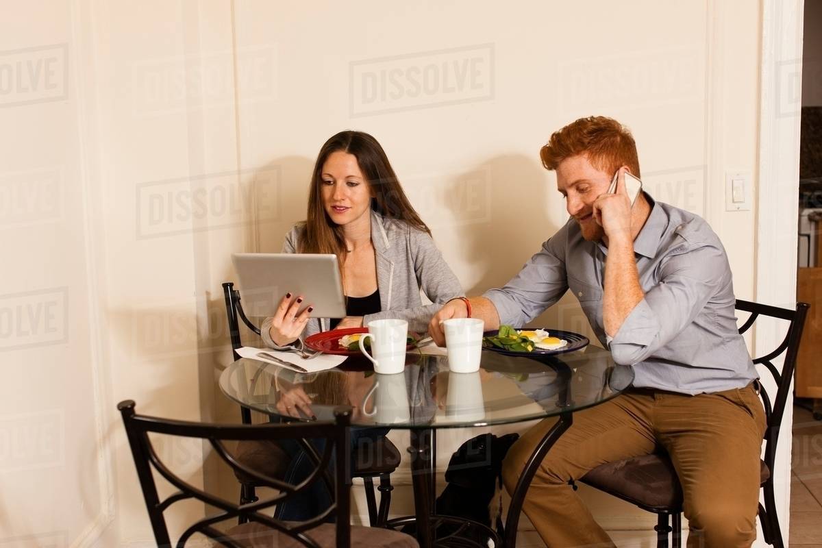 Couple at dining table using smartphone and digital tablet - Royalty ...