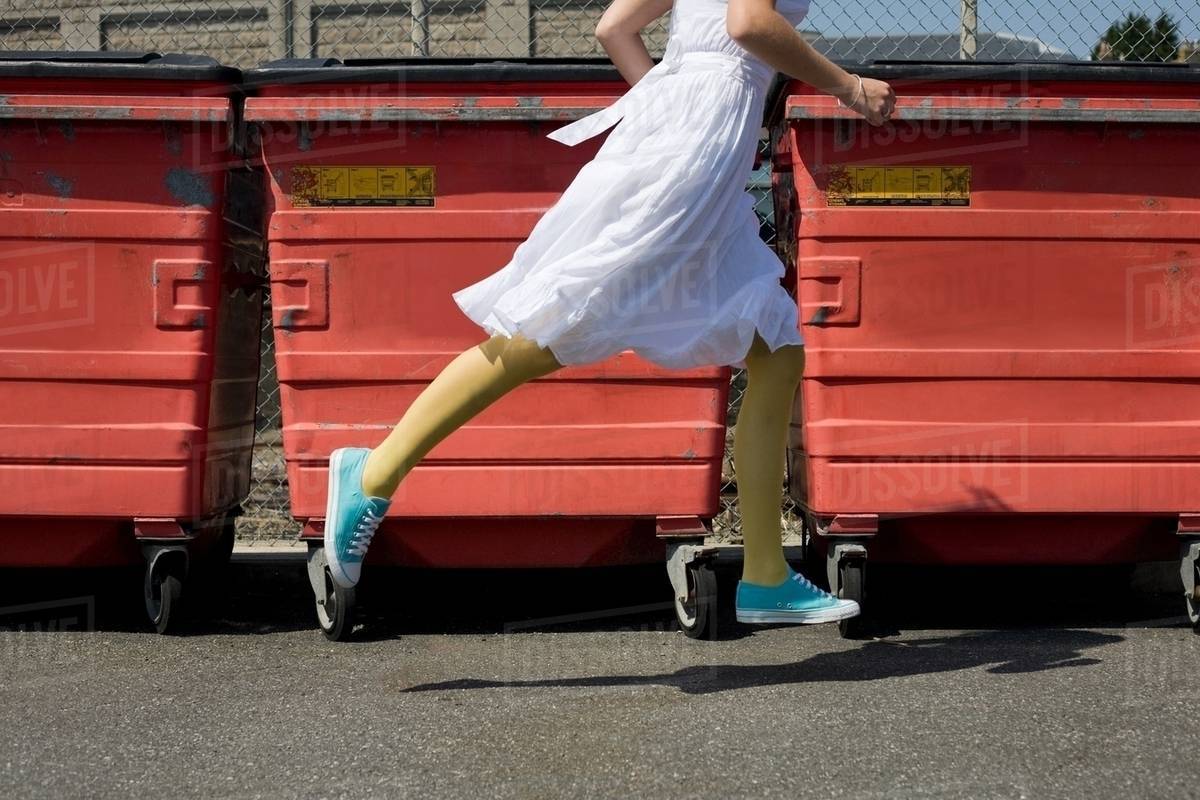 Woman running past wheelie bins - Royalty-free Stock Photo | Dissolve
