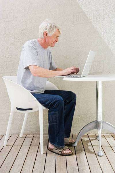 Middle aged man sitting on desk and using laptop - Royalty-free Stock ...