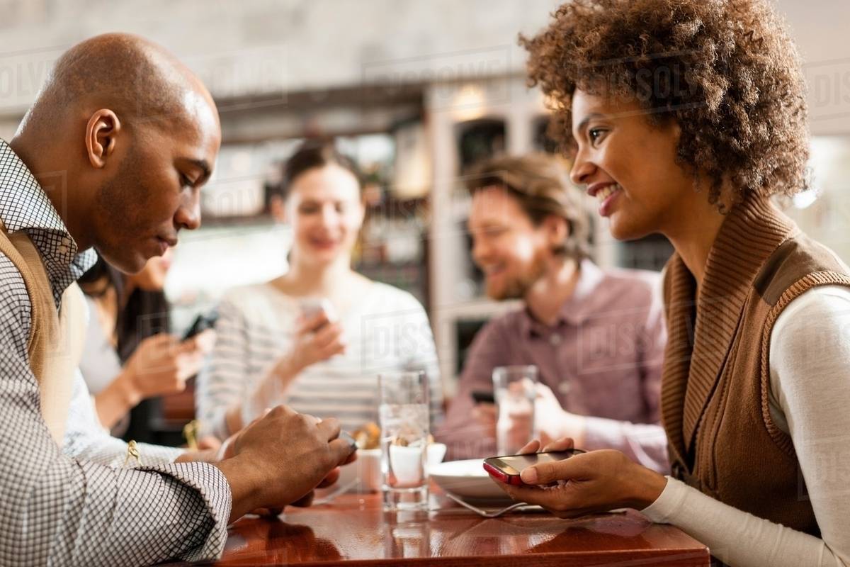 Friends at restaurant texting and showing photos using cell phones ...