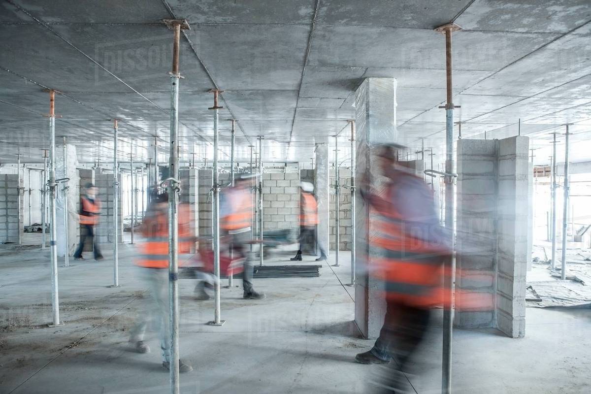Six blurred construction workers on the go in busy construction site ...