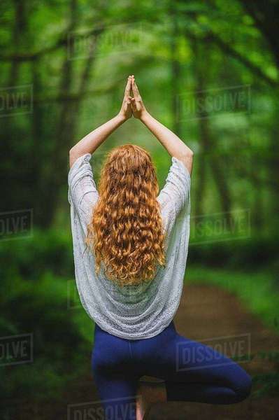 Rear view of young woman in forest practicing yoga in tree pose ...