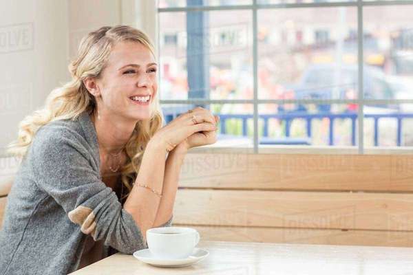 Young woman sitting at table with tea and saucer, resting on elbows ...