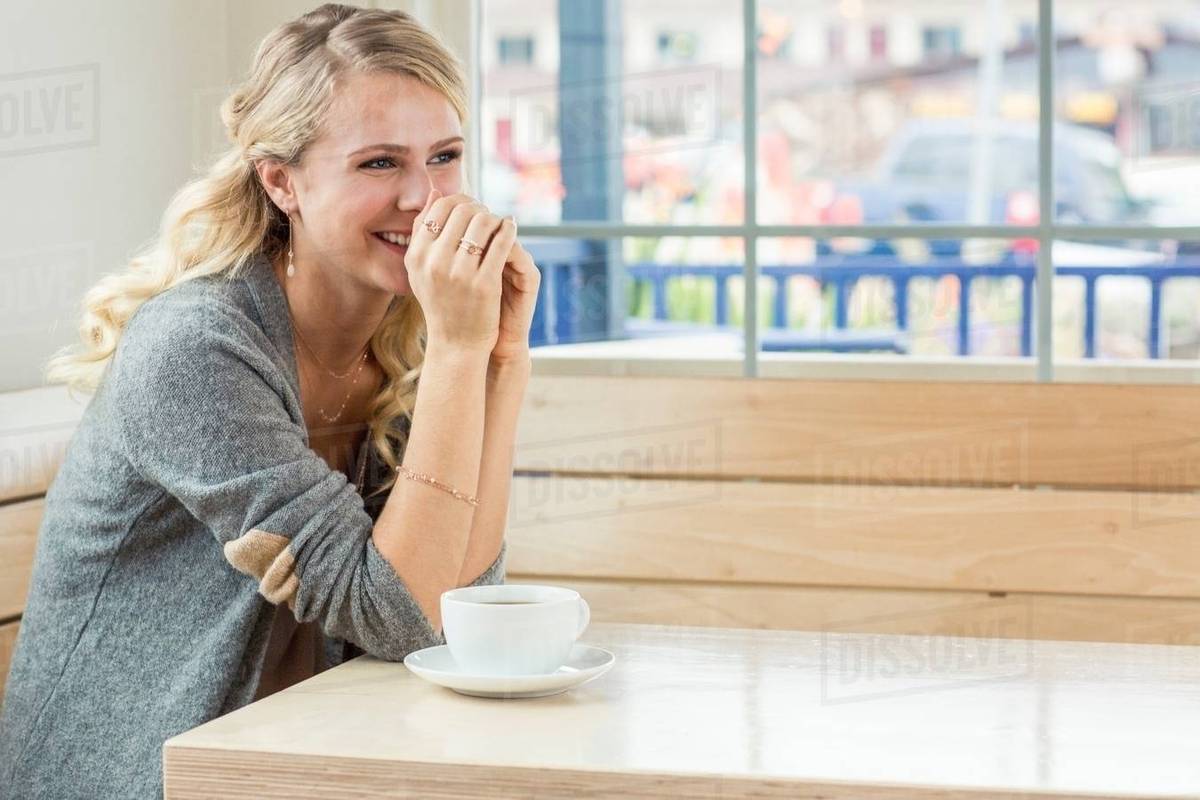 Young woman sitting at table with tea and saucer, resting on elbows ...