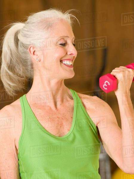 Older woman lifting weights at home - Stock Photo - Dissolve