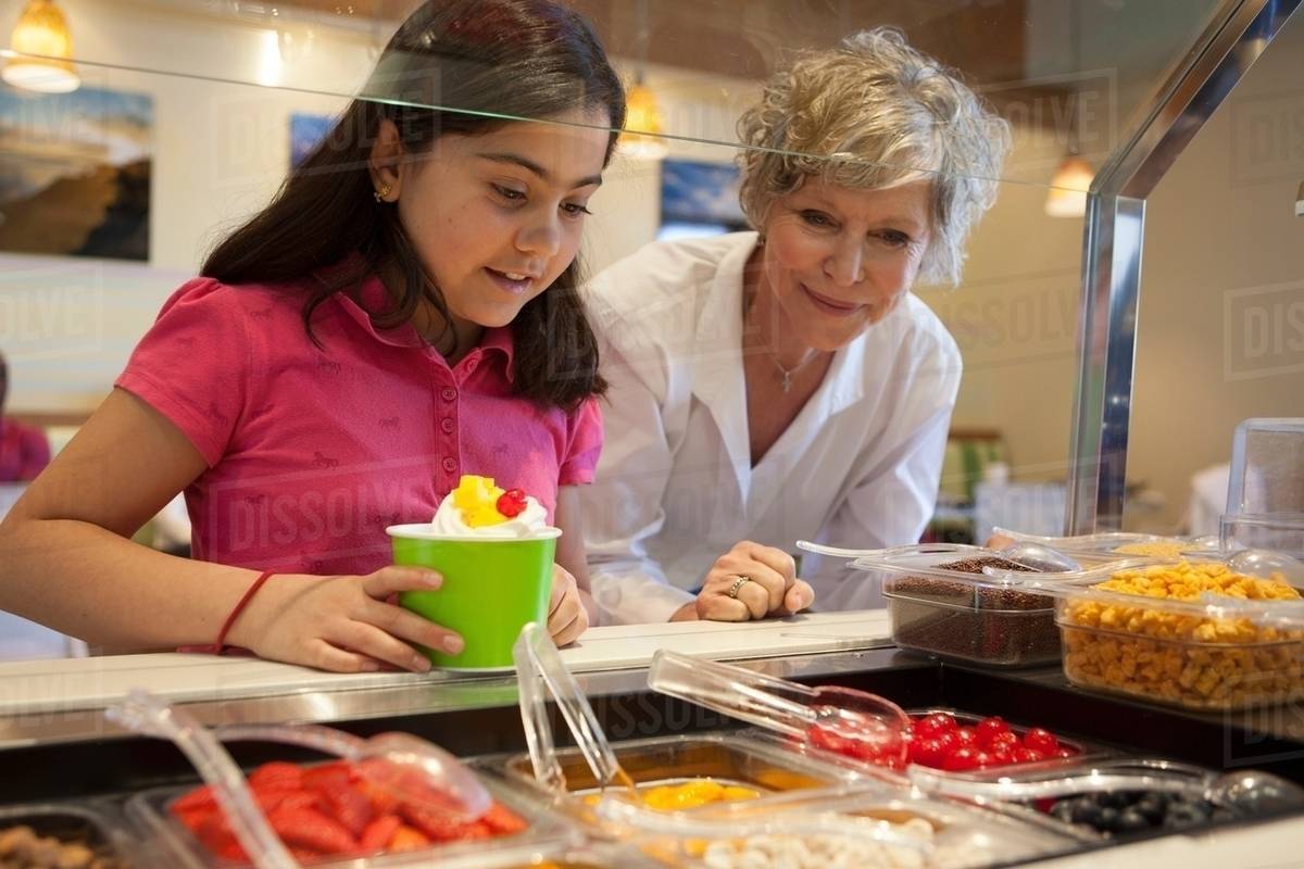 Girl putting toppings on frozen yogurt - Stock Photo - Dissolve