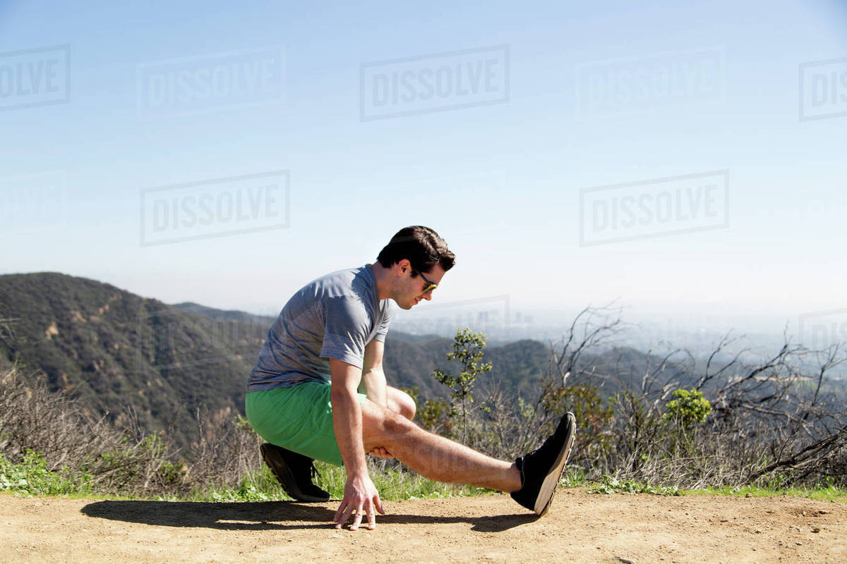Man crouching on mountain doing leg stretching exercise - Stock Photo ...