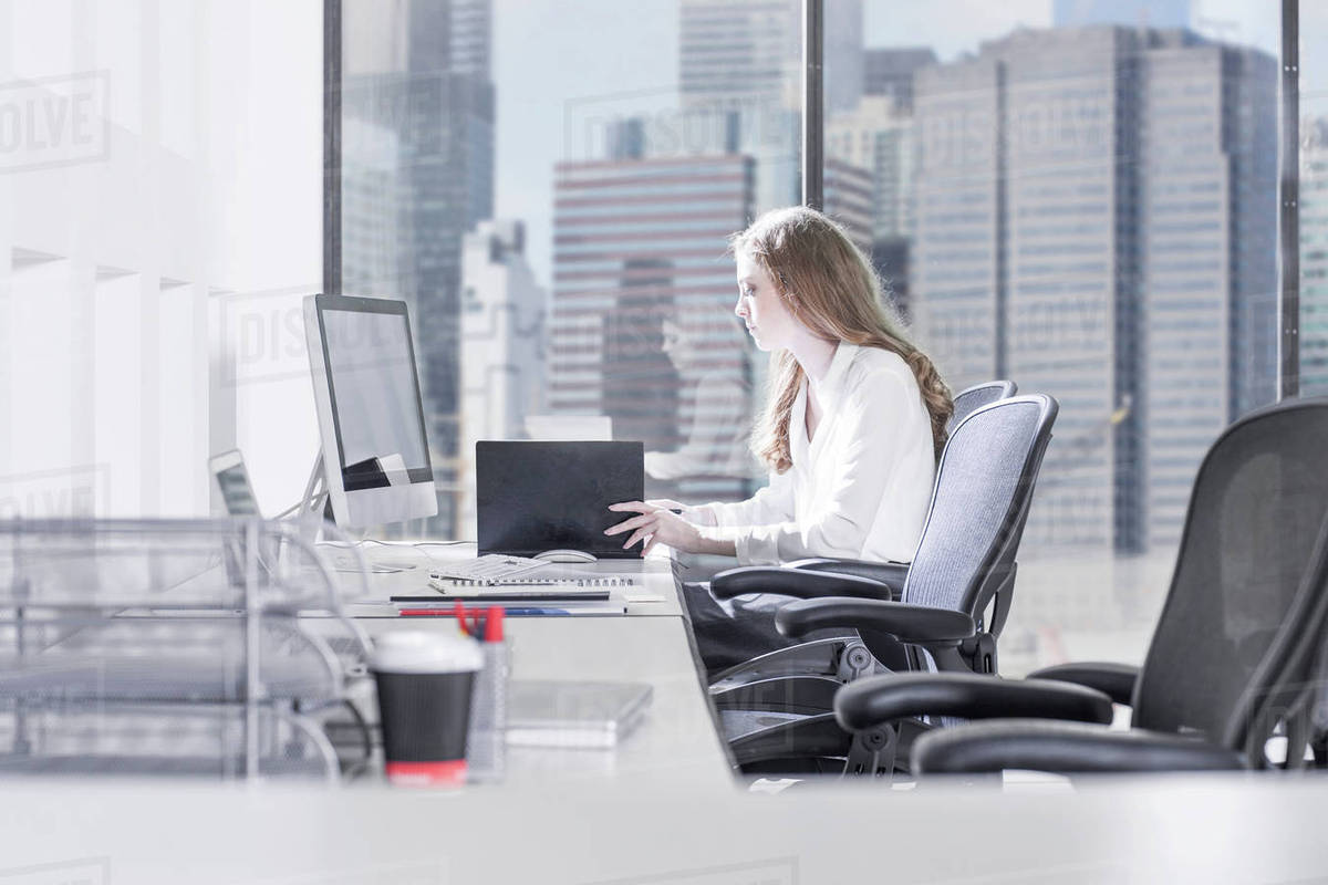 Businesswoman writing notes and using computer in front of office ...