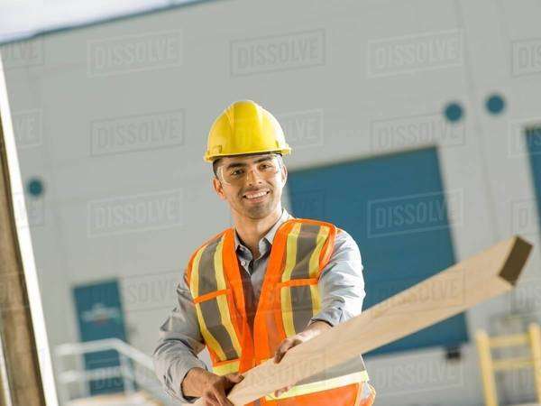 Mid adult construction worker holding wood - Stock Photo - Dissolve