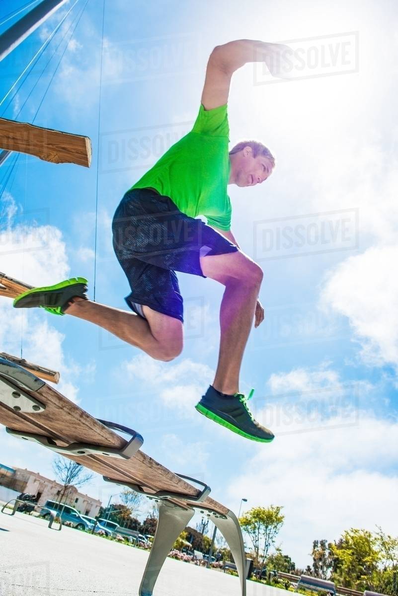 Young man leaping over park bench in city - Stock Photo - Dissolve