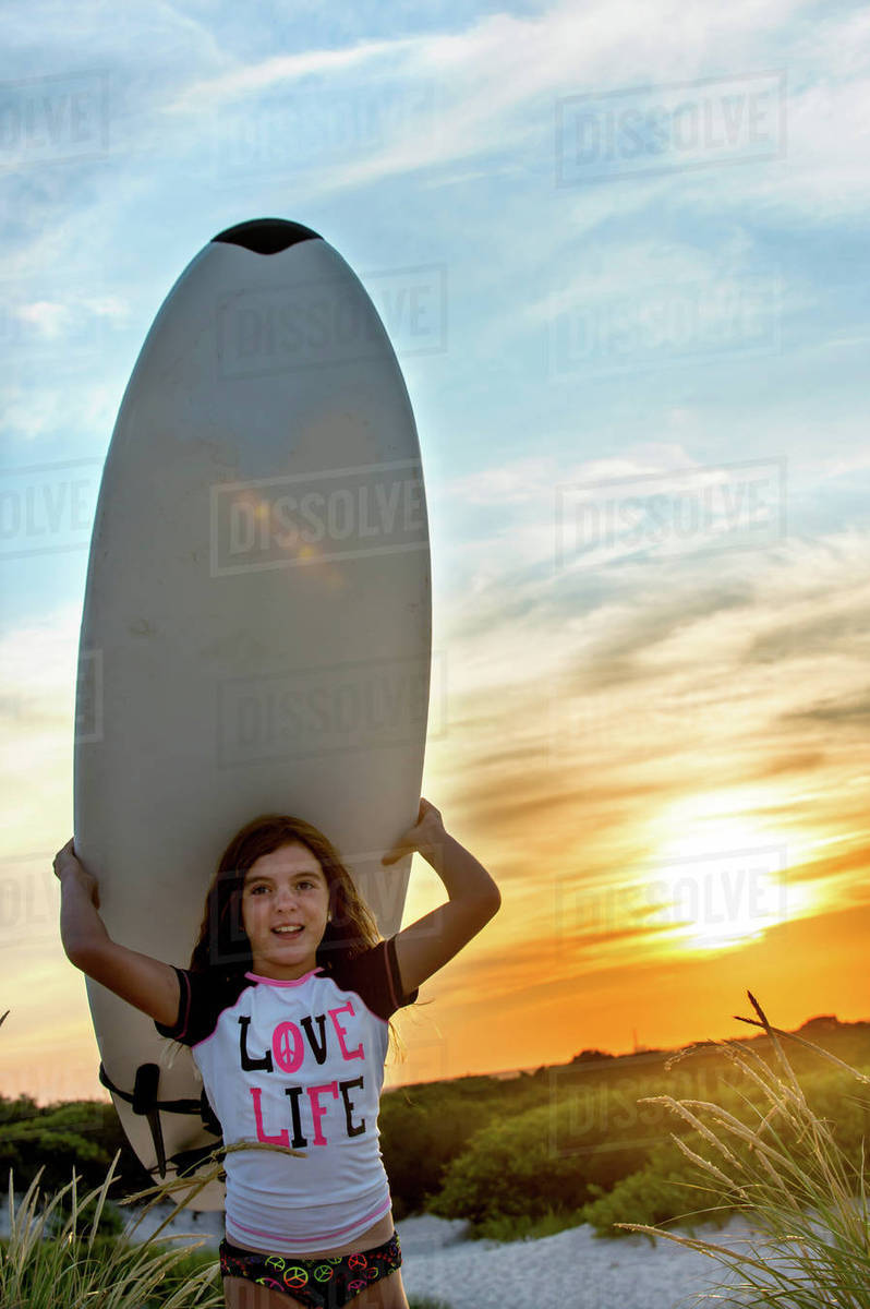 Young girl at beach, carrying surfboard, at sunset - Royalty-free Stock ...