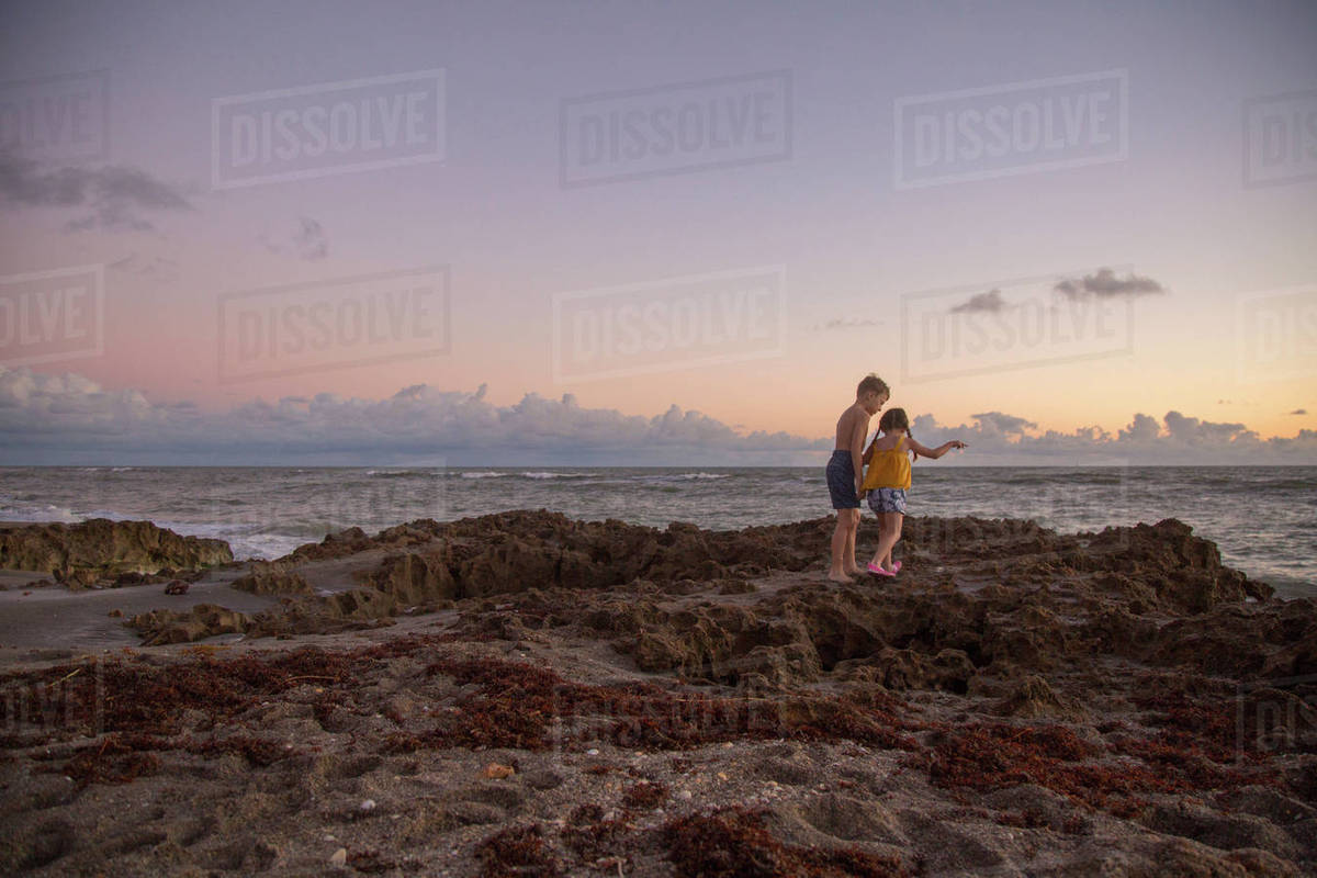 Girl and brother stepping over beach rocks at sunrise, Blowing Rocks ...