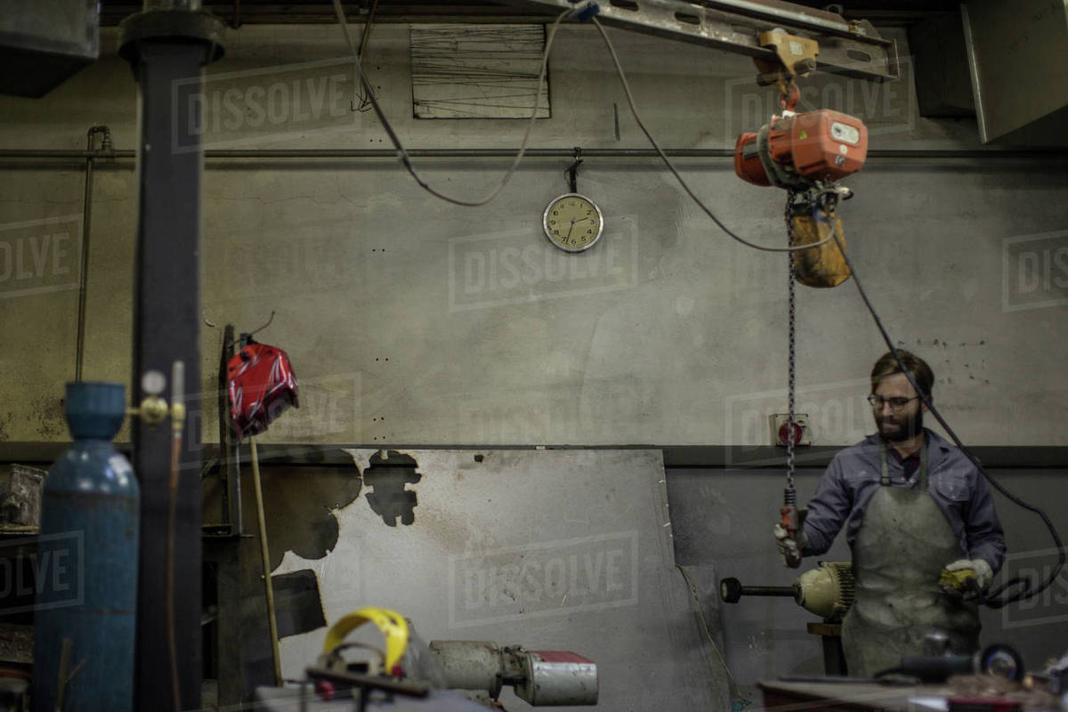 Man in workshop using chain hoist - Royalty-free Stock Photo | Dissolve