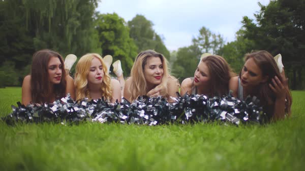 Portrait of happy cheerleading team lying on grass and talking ...