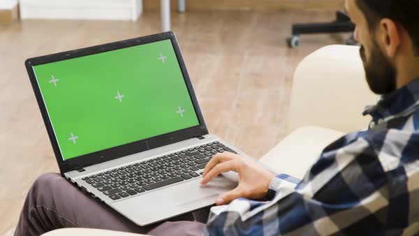 Man on the sofa looking at green screen laptop in a bright and well lit ...