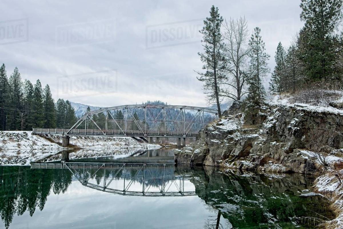 An older steel bridge spans across the calm Coeur d:Alene River in ...