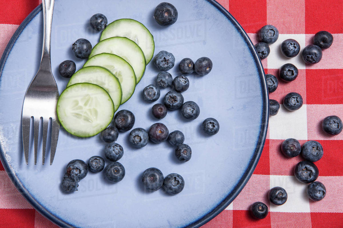 An overview of blueberries, sliced cucumbers, and a fork on a blue ...