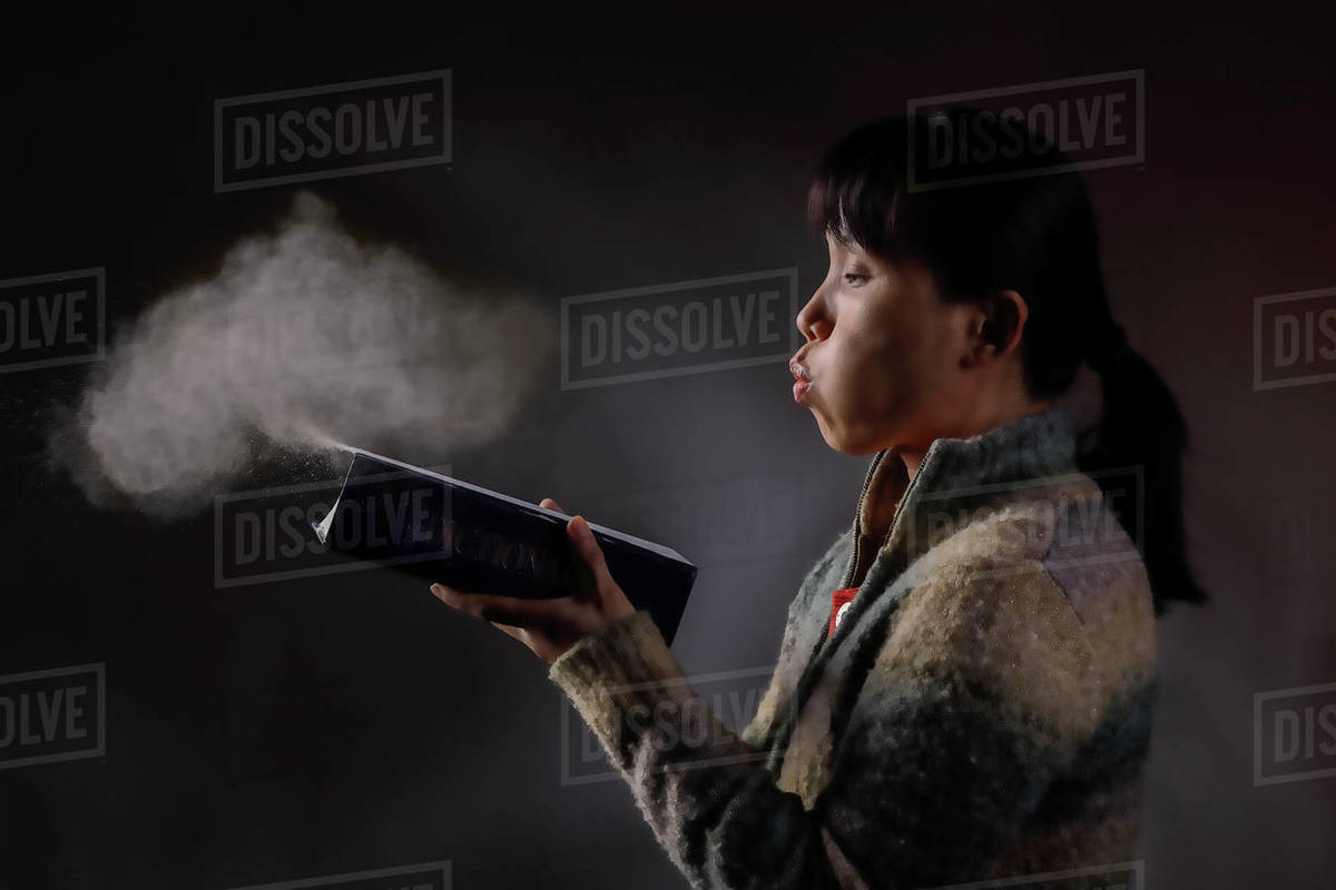 Asian woman blows dust off an old dictionary in this concept image ...