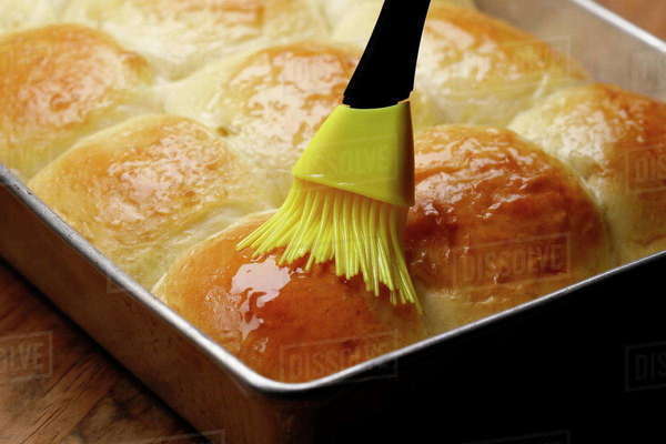 Applying butter on top of freshly baked home made dinner rolls ...