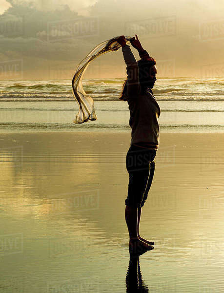 A woman lets a scarf blow in the wind at sunset on the beach in Newport ...