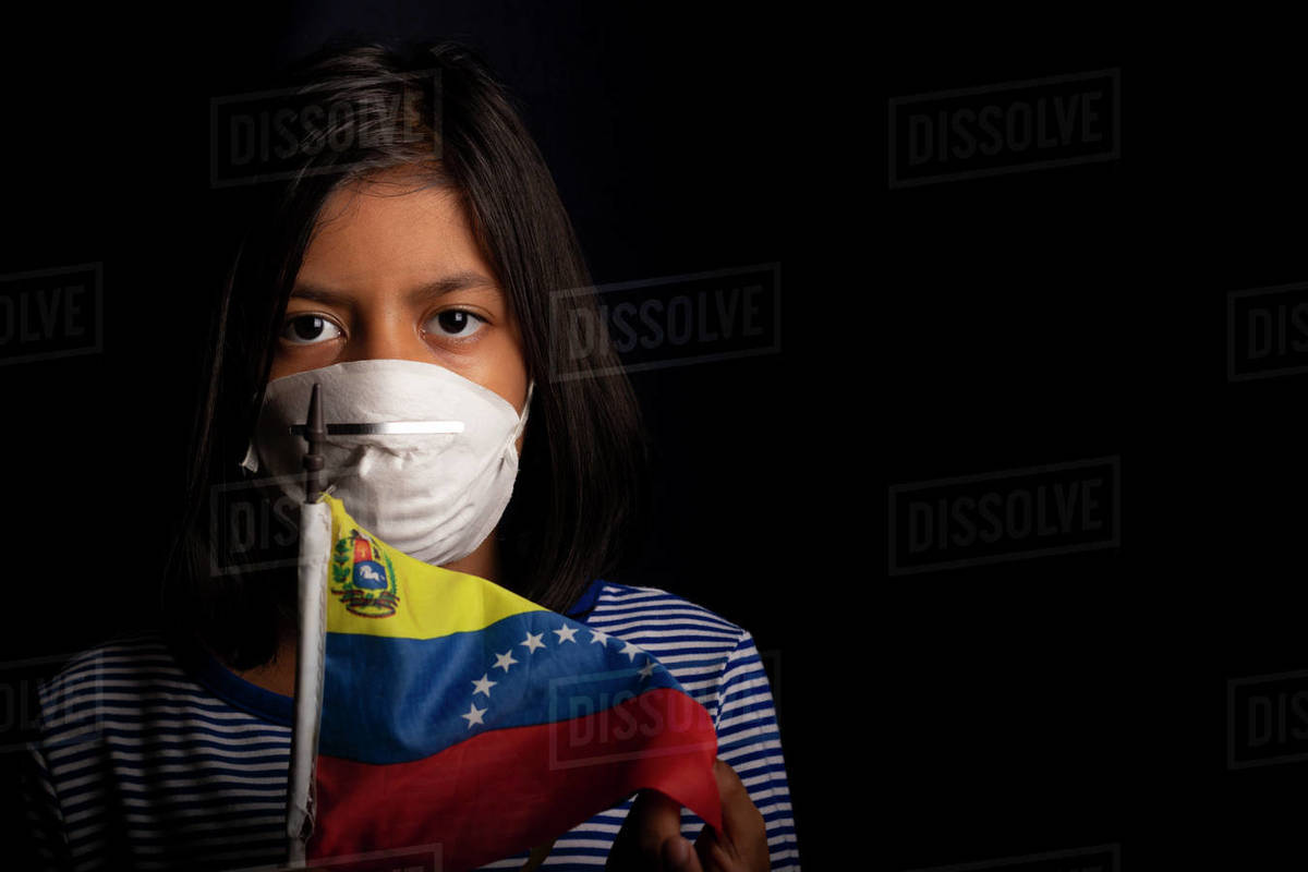 Portrait of little Venezuelan girl wearing medical mask and holding ...