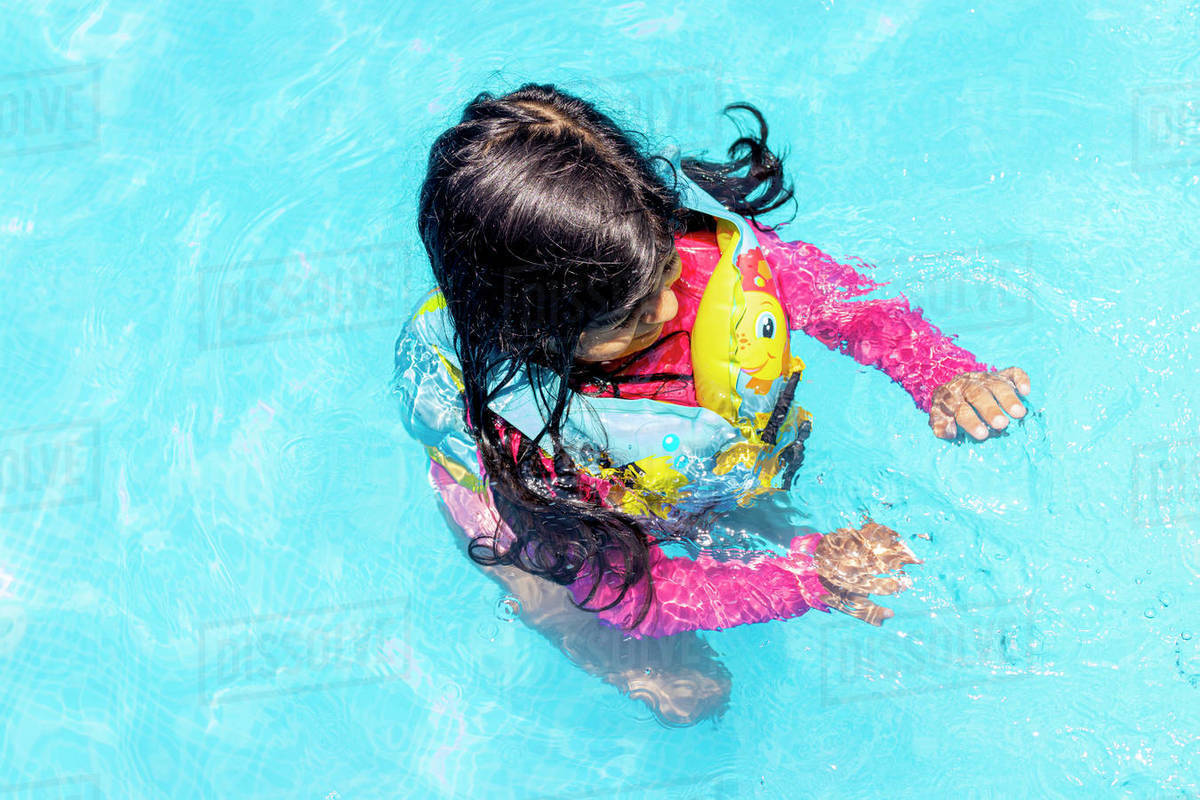 Little girl swimming with floaties, in the blue waters of a pool in the ...