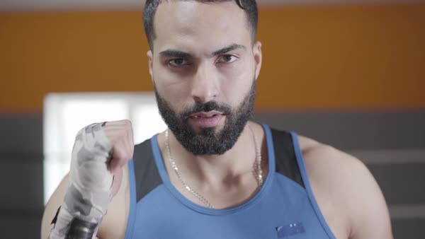 Close-up of brown-eyed Middle Eastern boxer pointing at camera and back ...