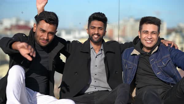 Three happy Middle Eastern men waving looking at camera smiling sitting ...