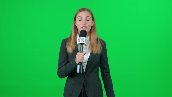 Female news reporter speaks into a microphone on a green background and ...