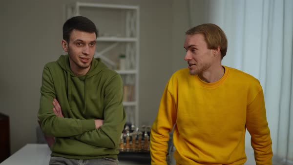 Two young relaxed men talking leaning on table smiling. Zoom in ...