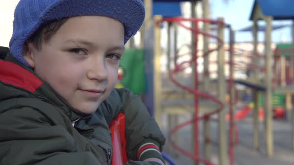 Close-up side view of sad lonely Caucasian boy sitting on playground in ...
