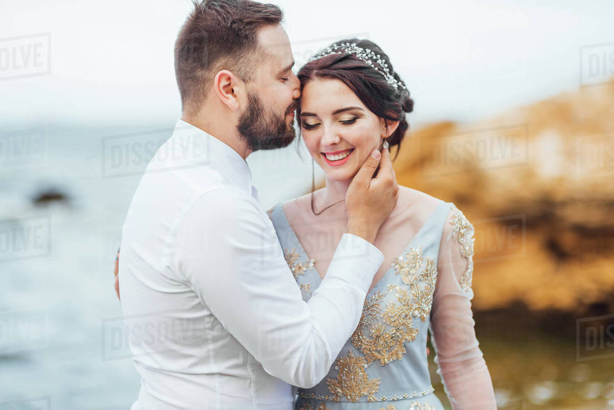 Same couple with a bride in a blue dress walk along the ocean shore ...
