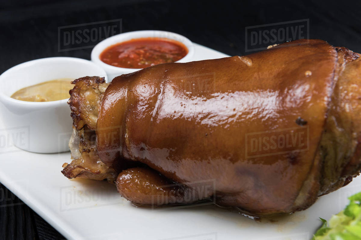 Tasty pork knuckle with sauces and vegetables on a white background ...