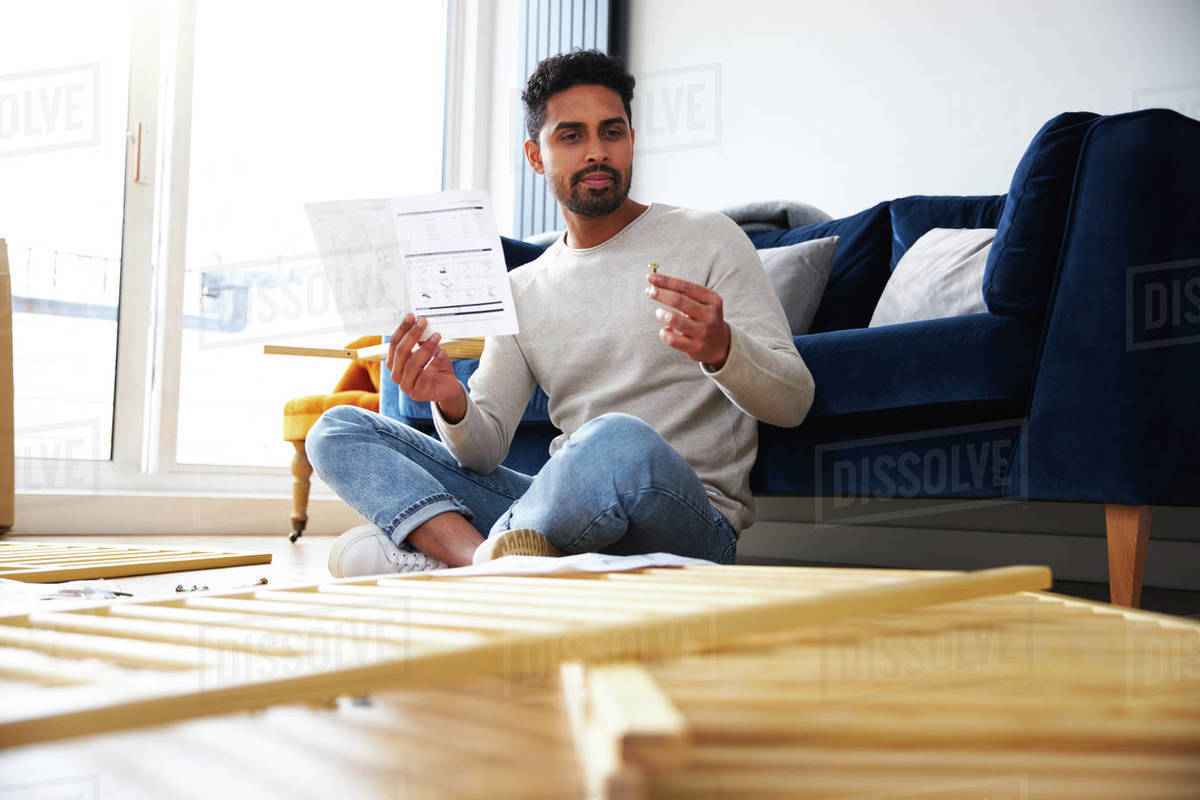 Confused man sitting on floor in lounge at home reading instructions ...