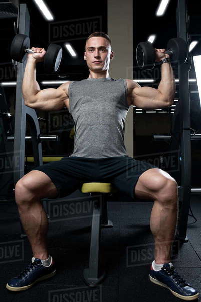 Muscular man doing dumbbell overhead press in the gym. Caucasian guy is ...