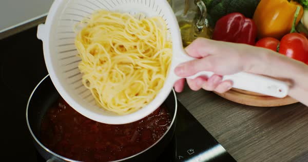 Pasta in tomato sauce in the process of cooking on the stove. A woman ...