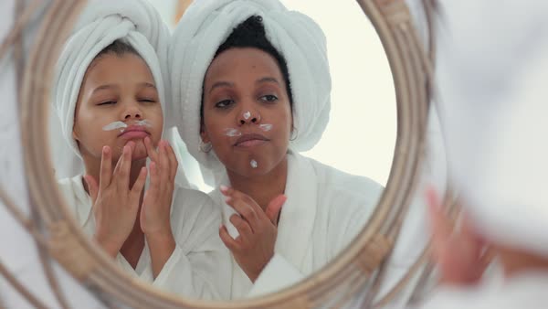 Mother, daughter are applying cream on skin of face and standing in ...