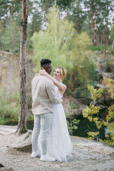 Happy interracial couple newlyweds stands, embraces and smiles against ...