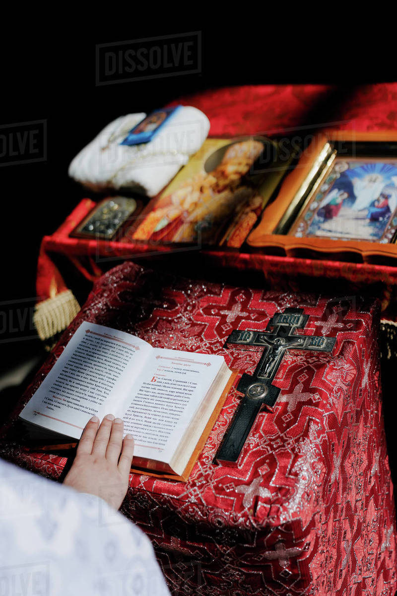 Hand of priest holds opened Holy Bible on the lectern near cross and ...