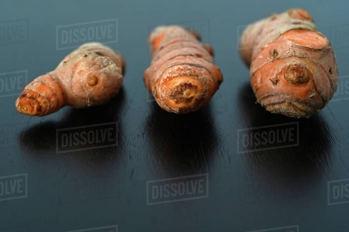 Three fresh organic Turmeric rhizome roots isolated on a black table ...