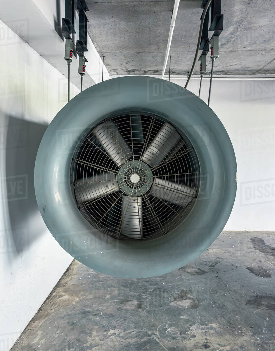 A large, gray, industrial fan is suspended from the ceiling of a ...