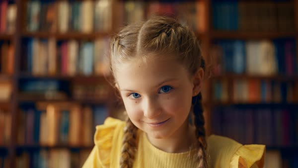 Portrait of smiling girl with blue eyes sitting in school library ...
