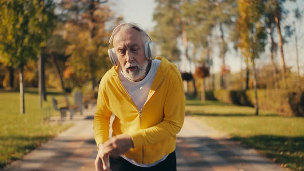 Senior man feeling breathless during jog in park, making stop to catch ...
